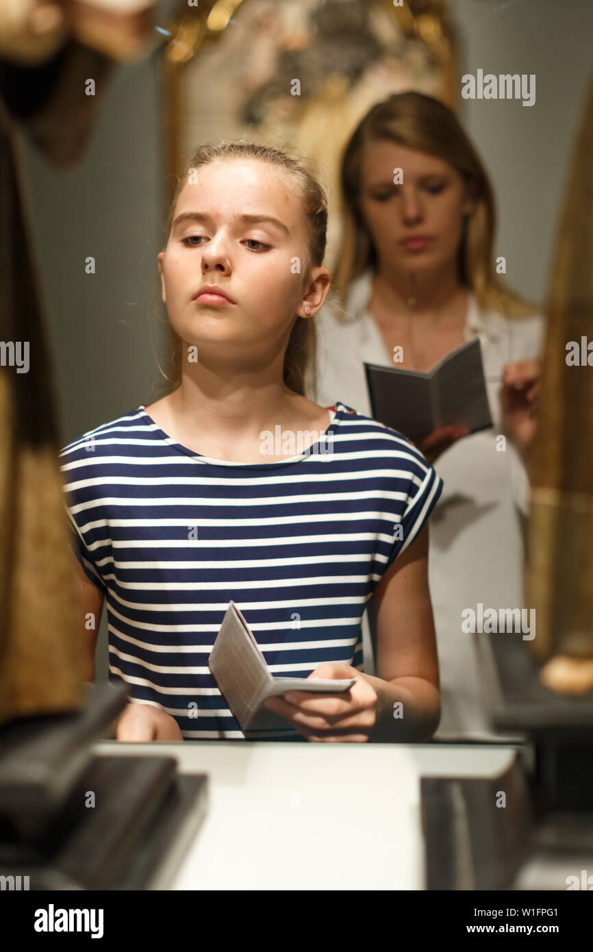 Girl looking at art objects in museum and using guidebook, mother on ...