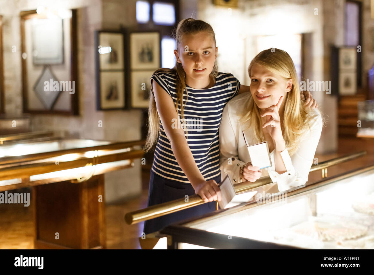 Girl with woman looking with interest at art objects under glass in ...