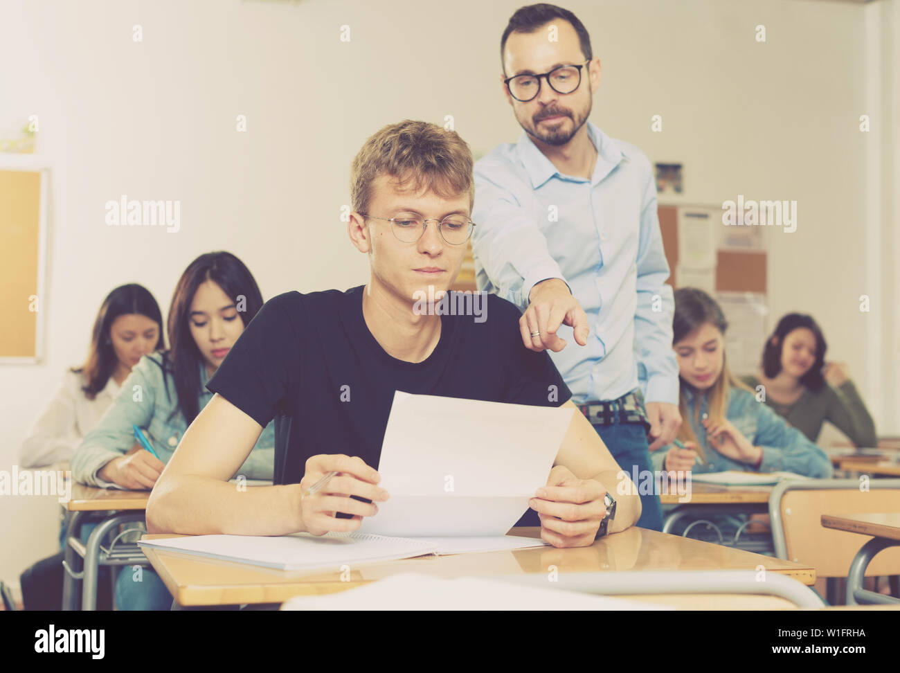 Schoolboy is writing answer the question on paper and teacher ...