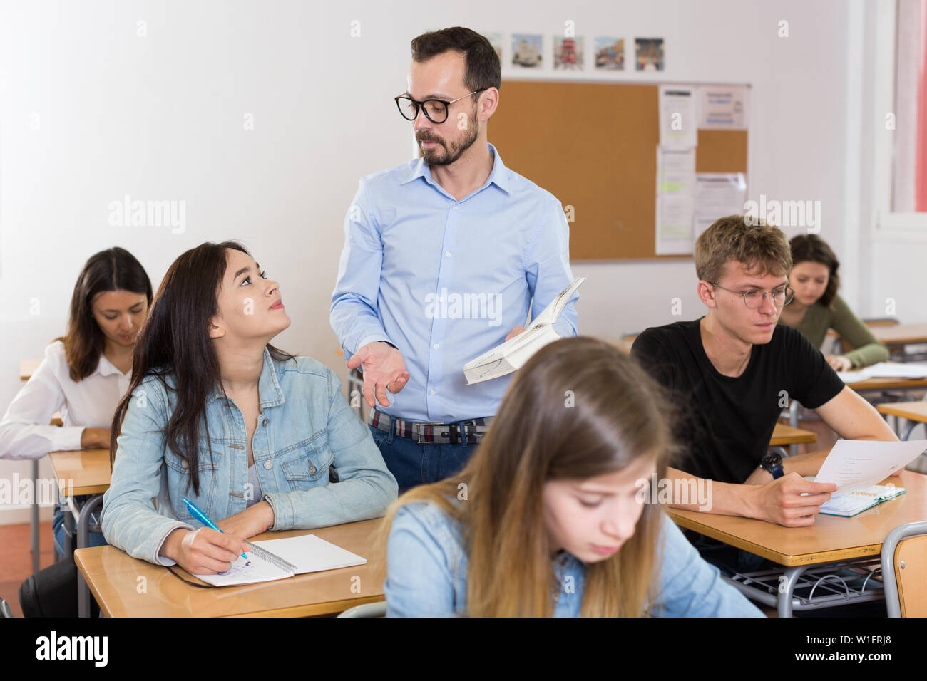 Young girl is writing test and teacher is explaining about questions in ...
