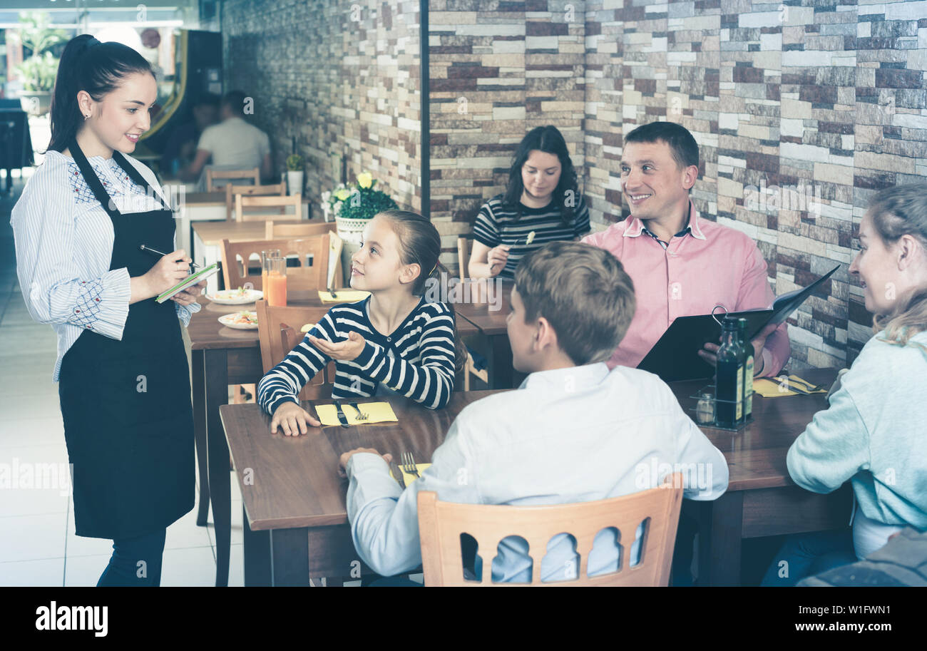 Positive adult waitress taking order from guests and writing into note ...