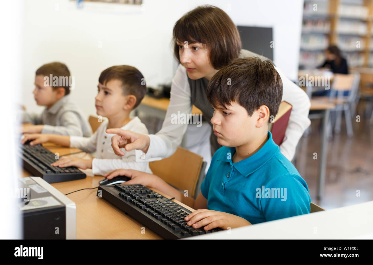 Young female teacher working with pupil in computer class of school ...