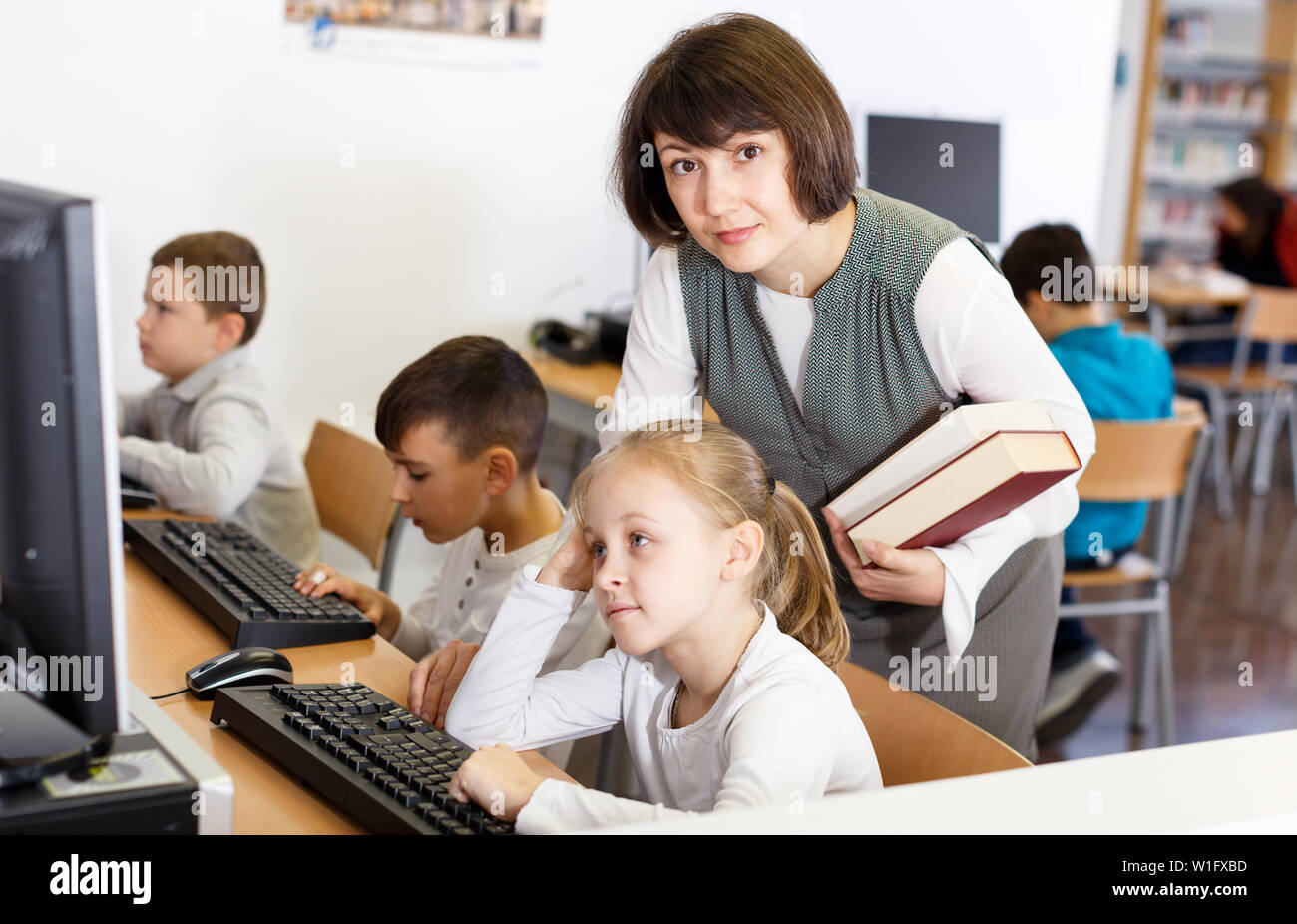 Young female teacher working with schoolgirl in computer class of ...