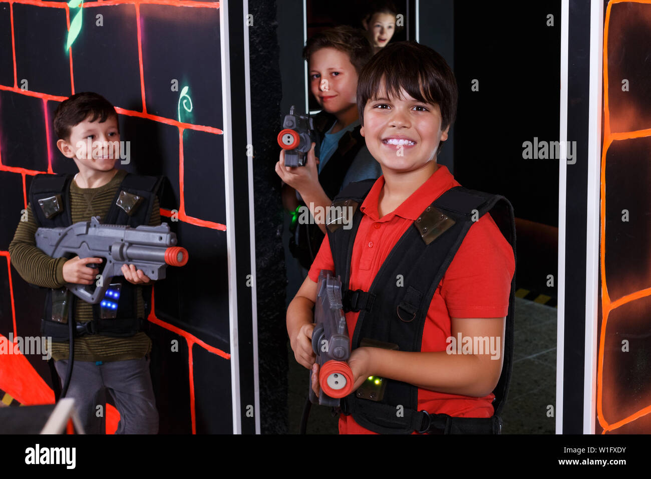 happy active boy aiming laser gun at other players during lasertag game ...