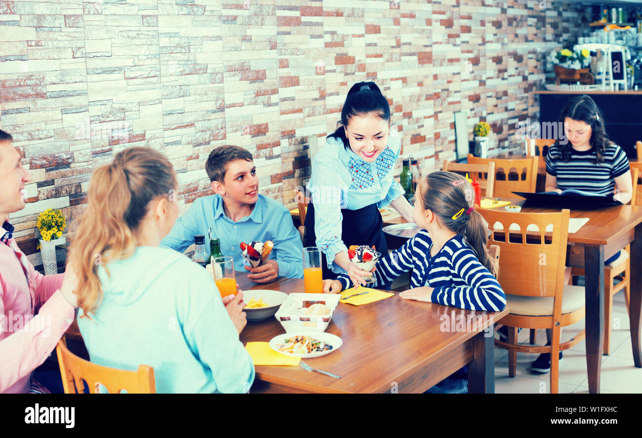 Woman is bringing delicious dessert to young visitors of family cafe ...