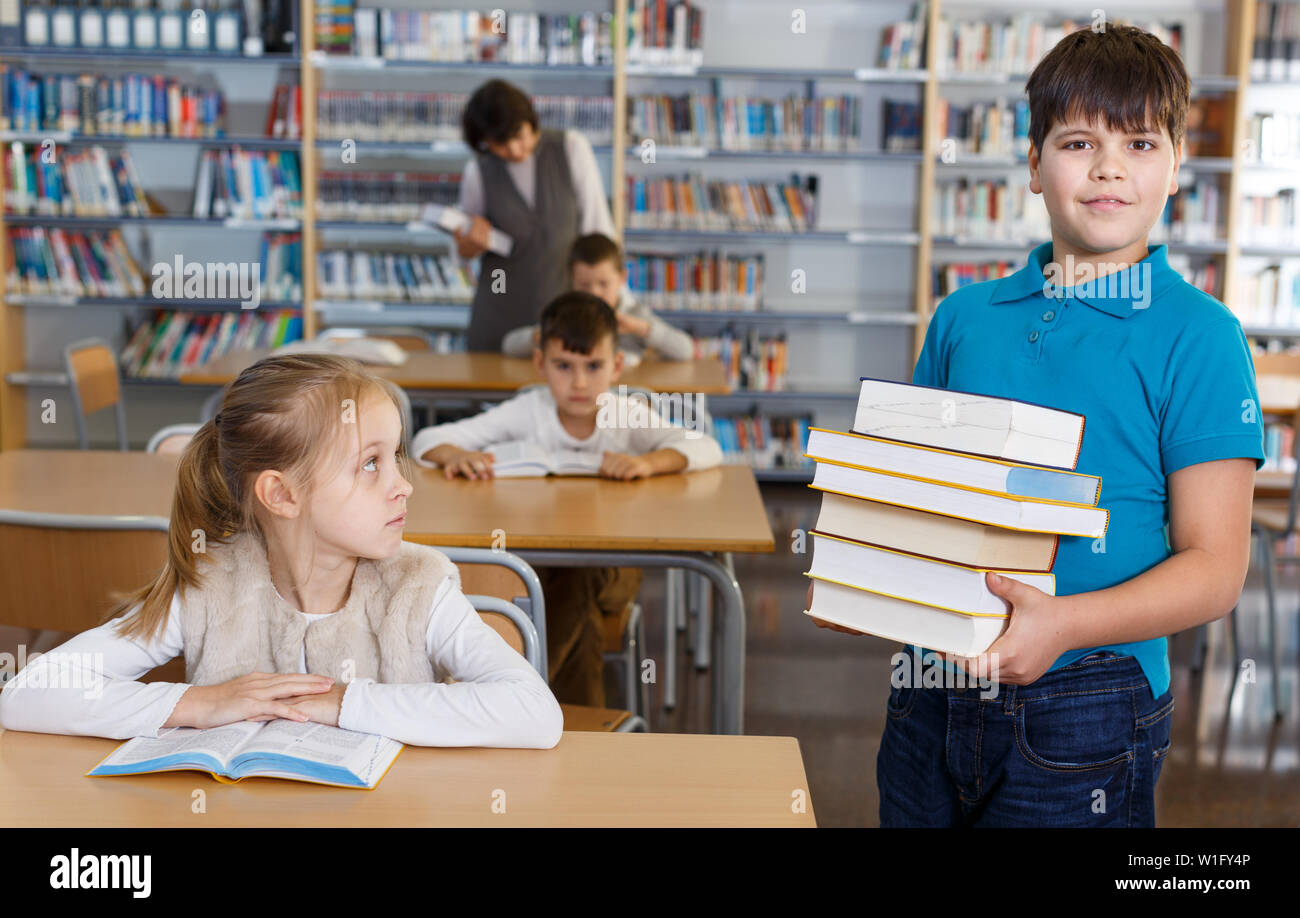 Portrait of happy tween boy standing in classroom with books in hands ...