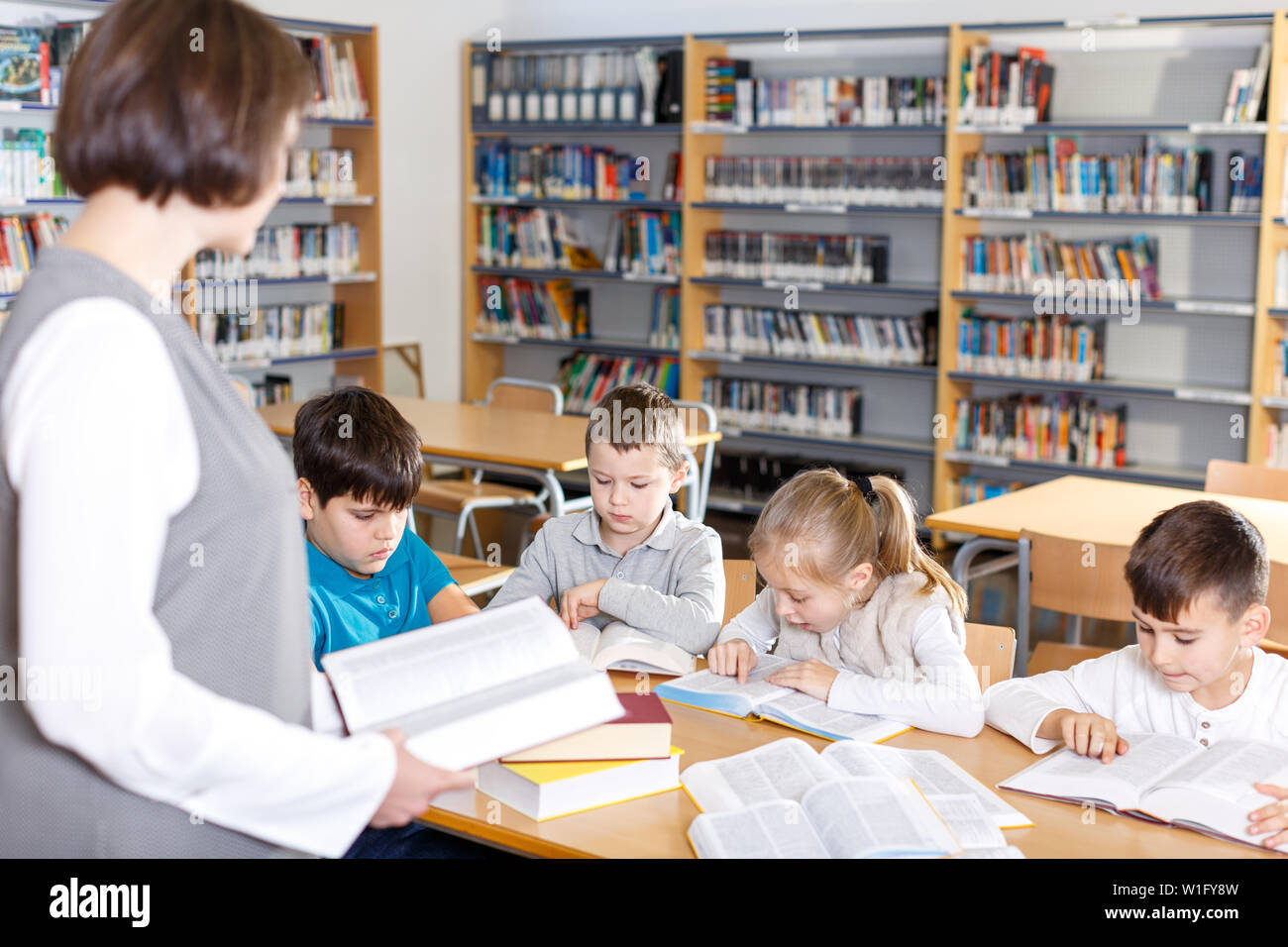 Group of school kids studying in school library with friendly female ...