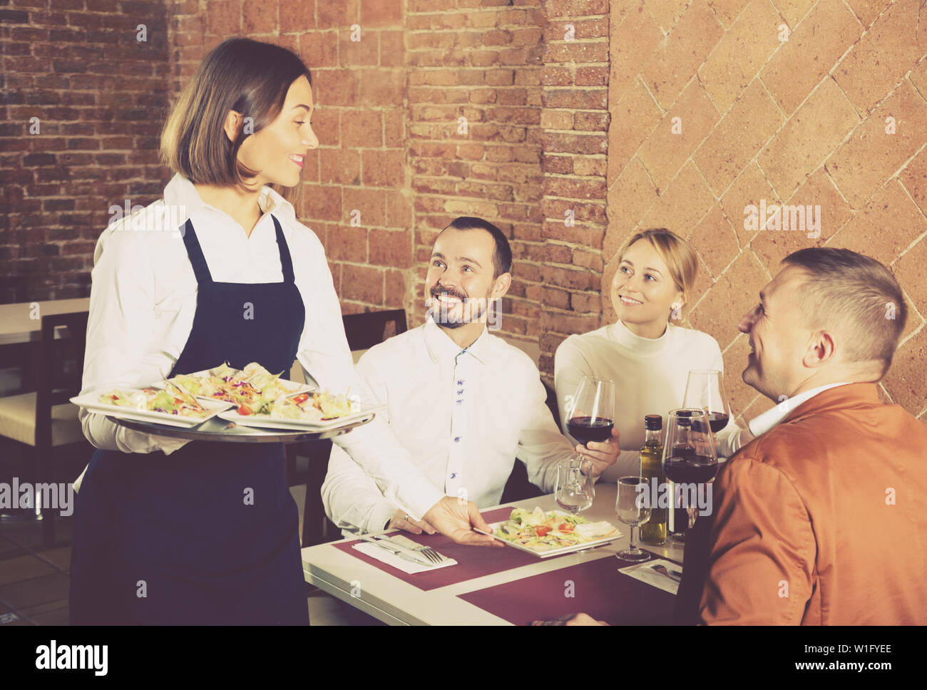 Happy female waitress placing order in front of guests in country ...