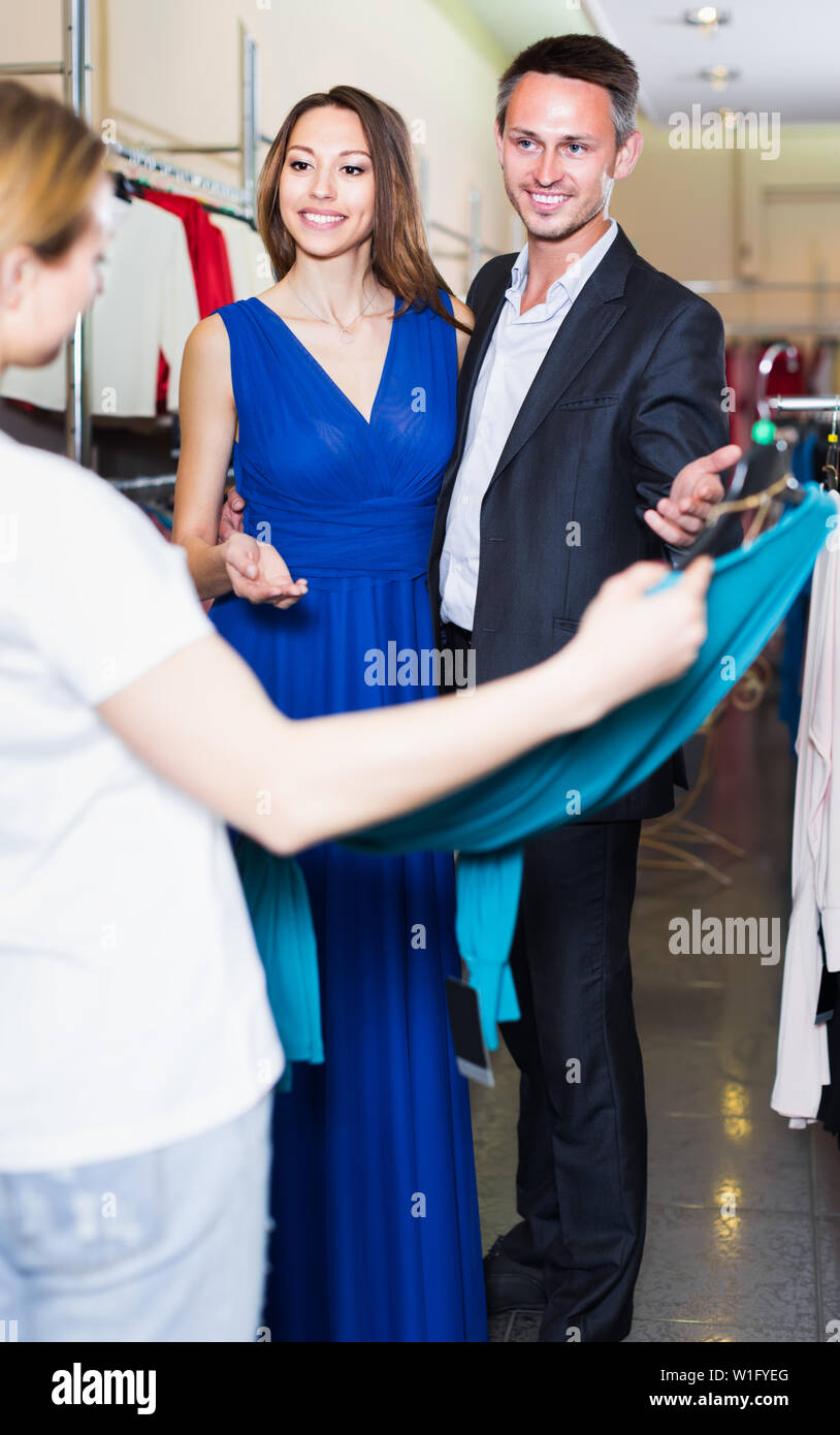 positive couple choosing new dress in the women's clothing shop with ...