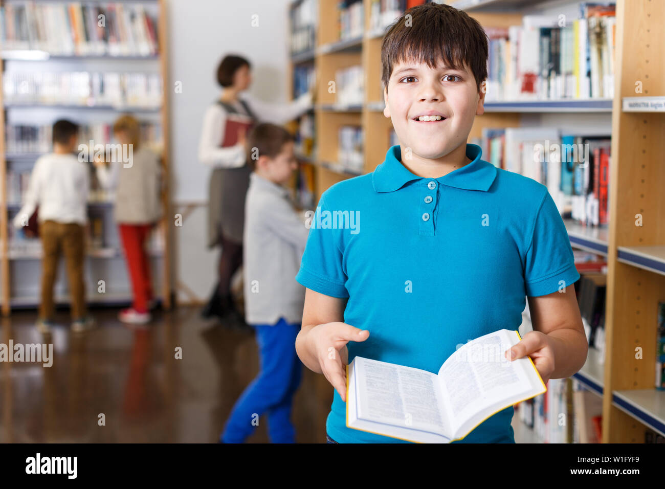 Portrait of happy tween boy holding open book in school library Stock ...