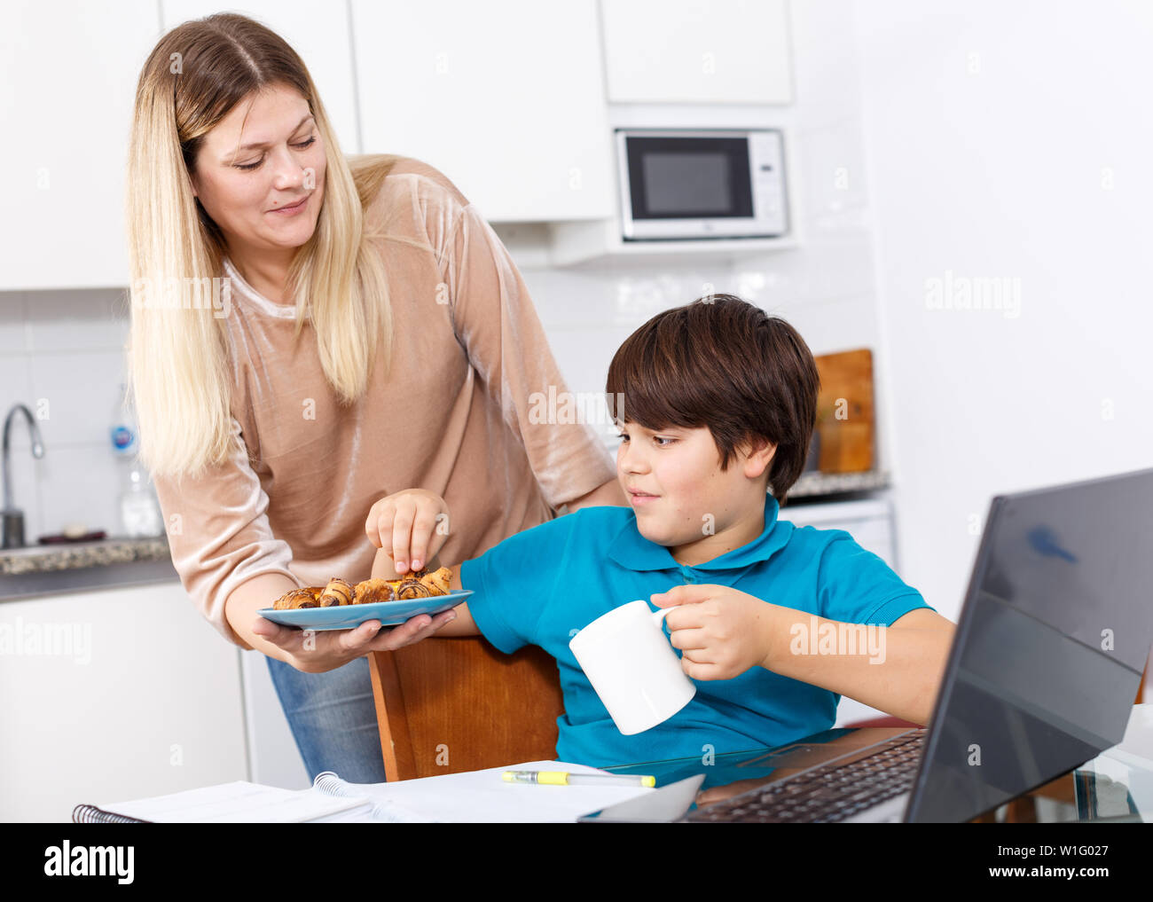 Positive woman serving breakfast to tween son sitting at table and ...