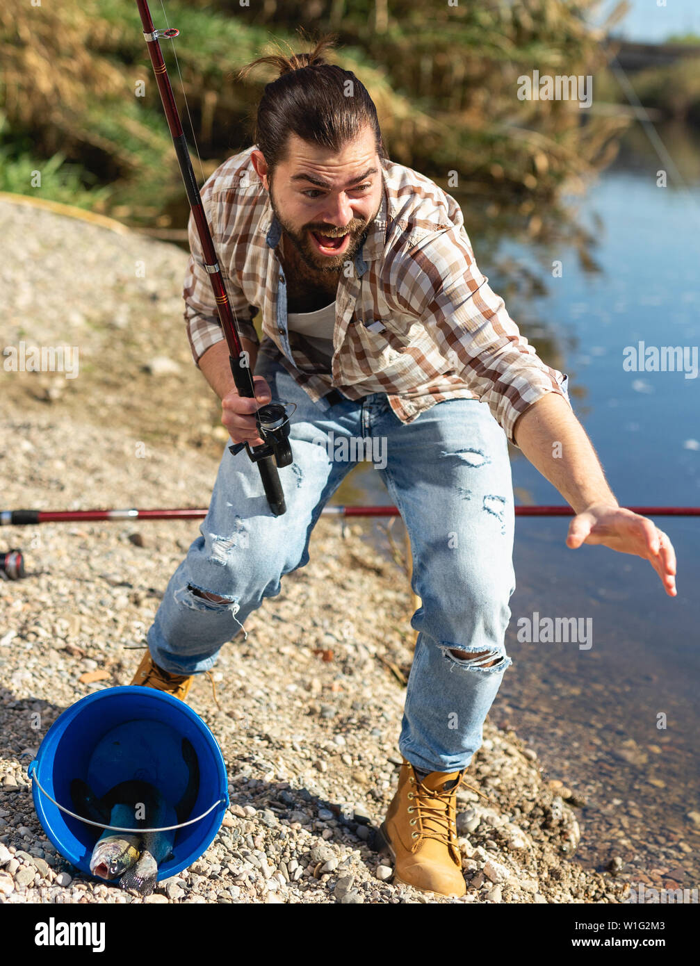 Adult man standing near river and pulling fish expressing emotions of ...