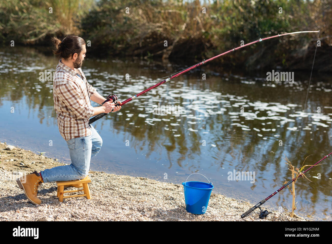 Adult man standing near river and pulling fish expressing emotions of ...