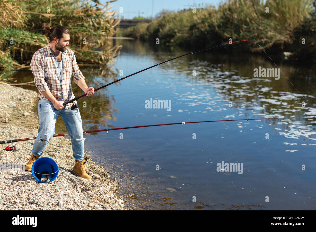 Adult man standing near river and pulling fish expressing emotions of ...