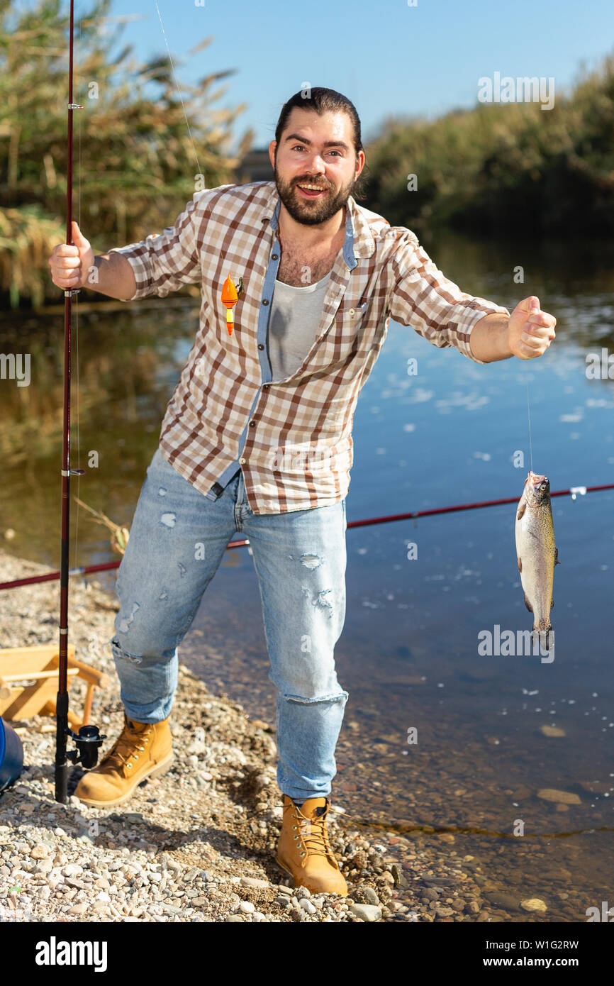 Adult man standing near river and pulling fish expressing emotions of ...