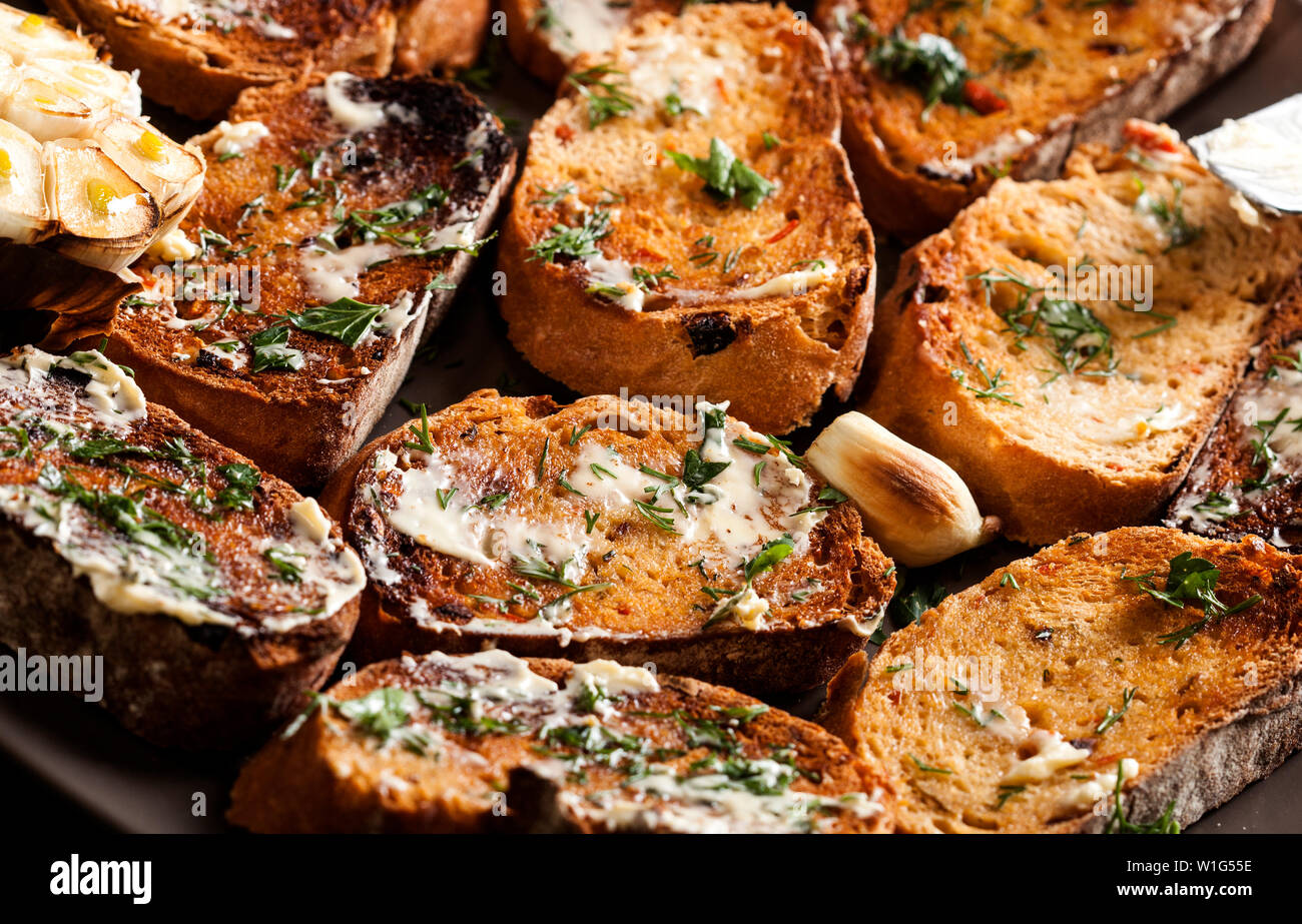 Sliced traditional toast bread with butter, garlic and herbs on a brown ...