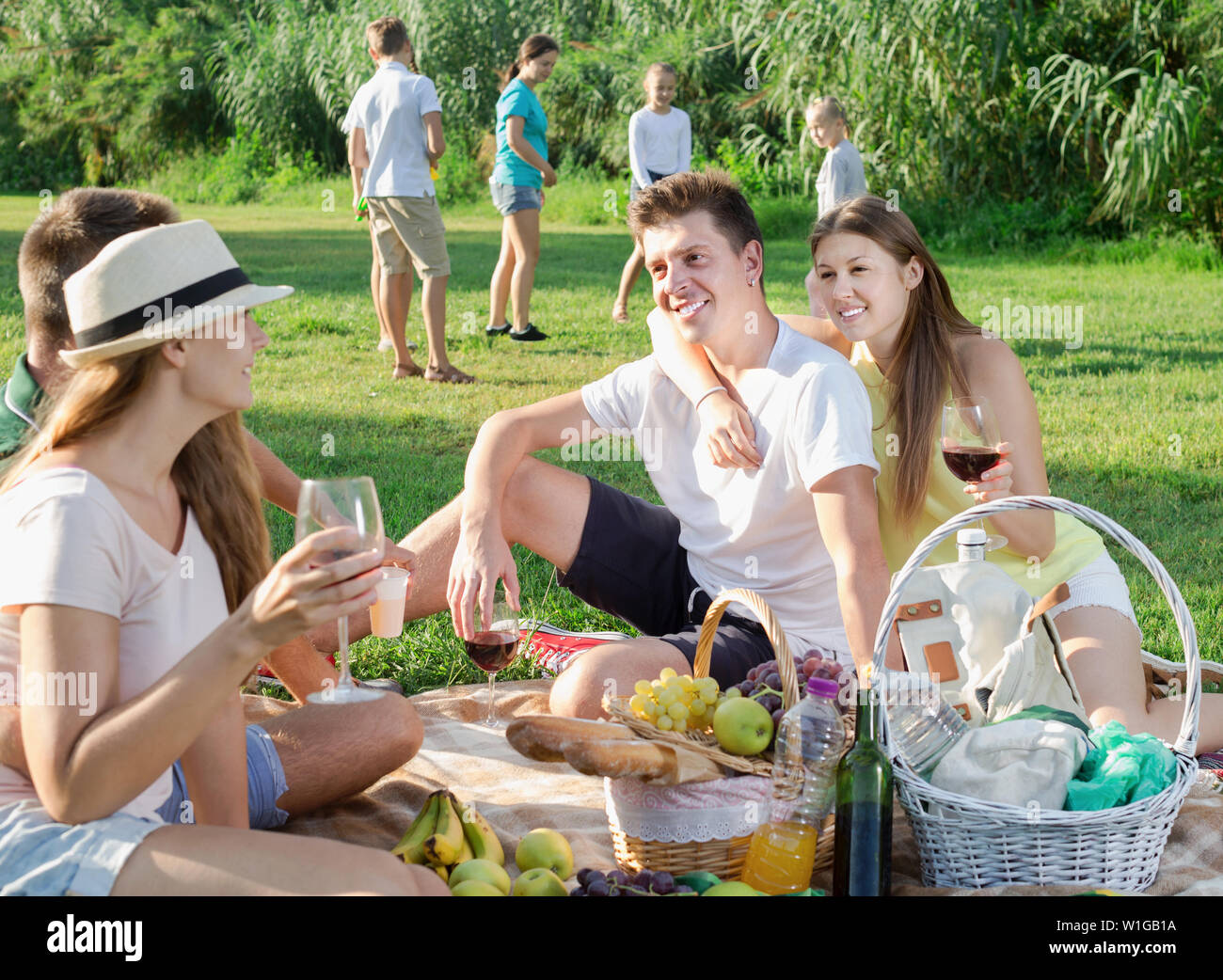 Happy four people on picnic outdoors on background with kids playing ...