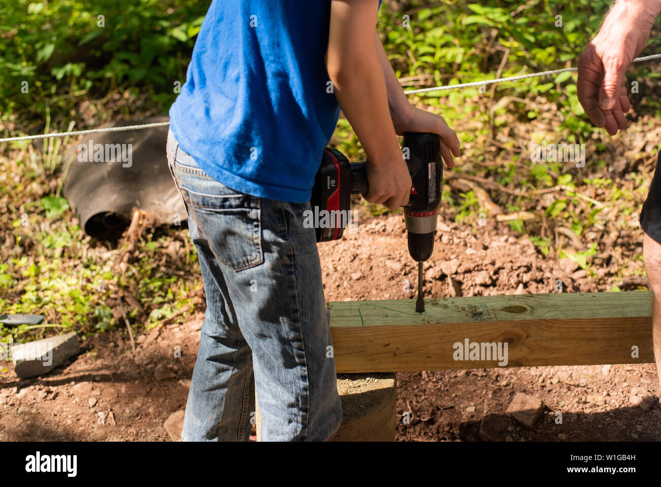 A young boy drills a hole in a board during a home improvement project ...