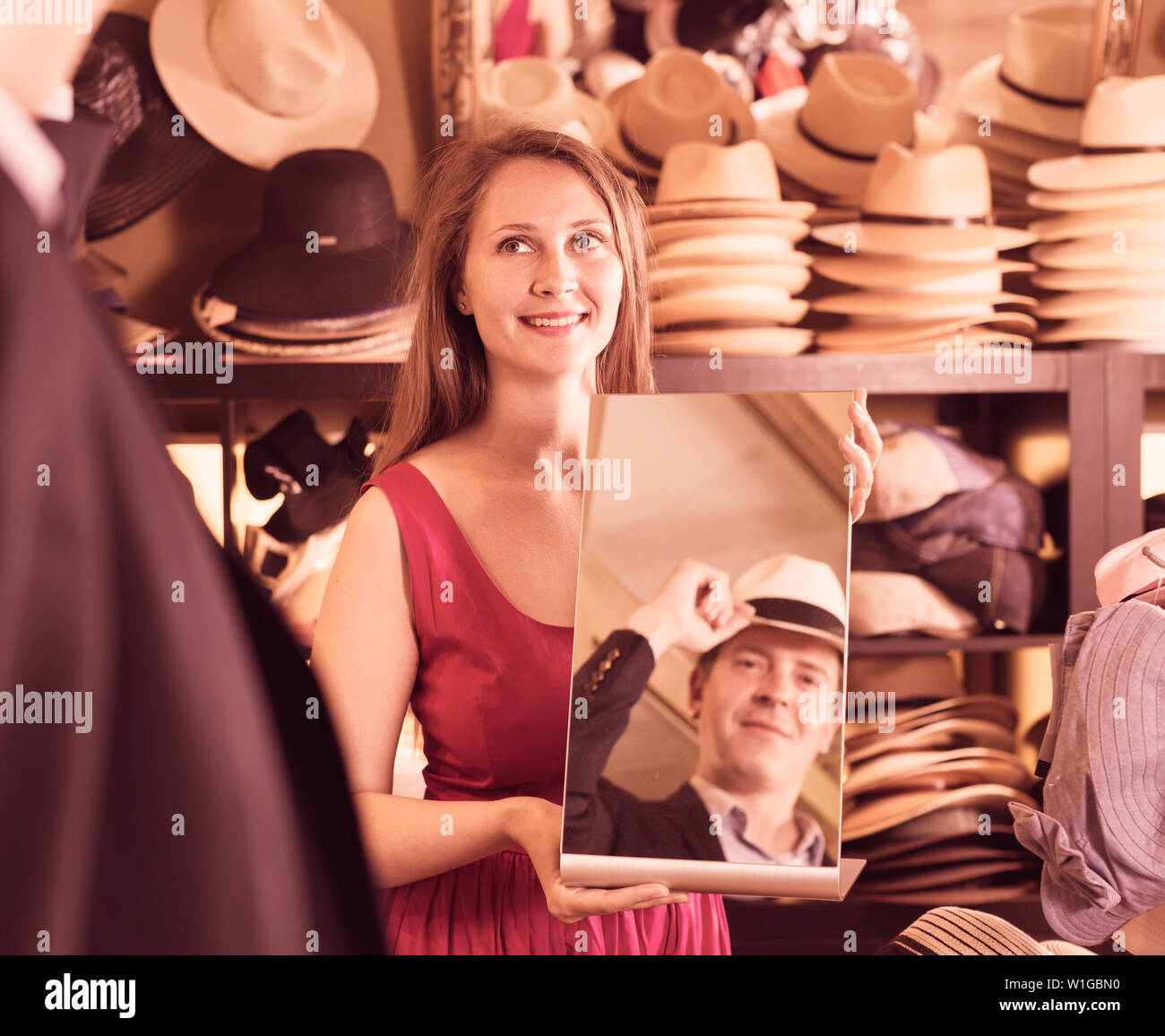 happy russian woman holding mirror and showing customer his reflection in hats shop Stock Photo ...