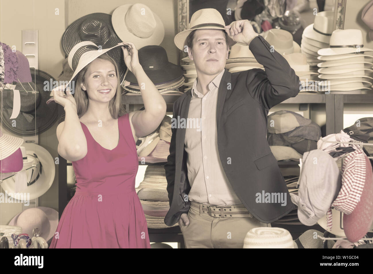attractive young female and man choosing hats from the assortment in ...