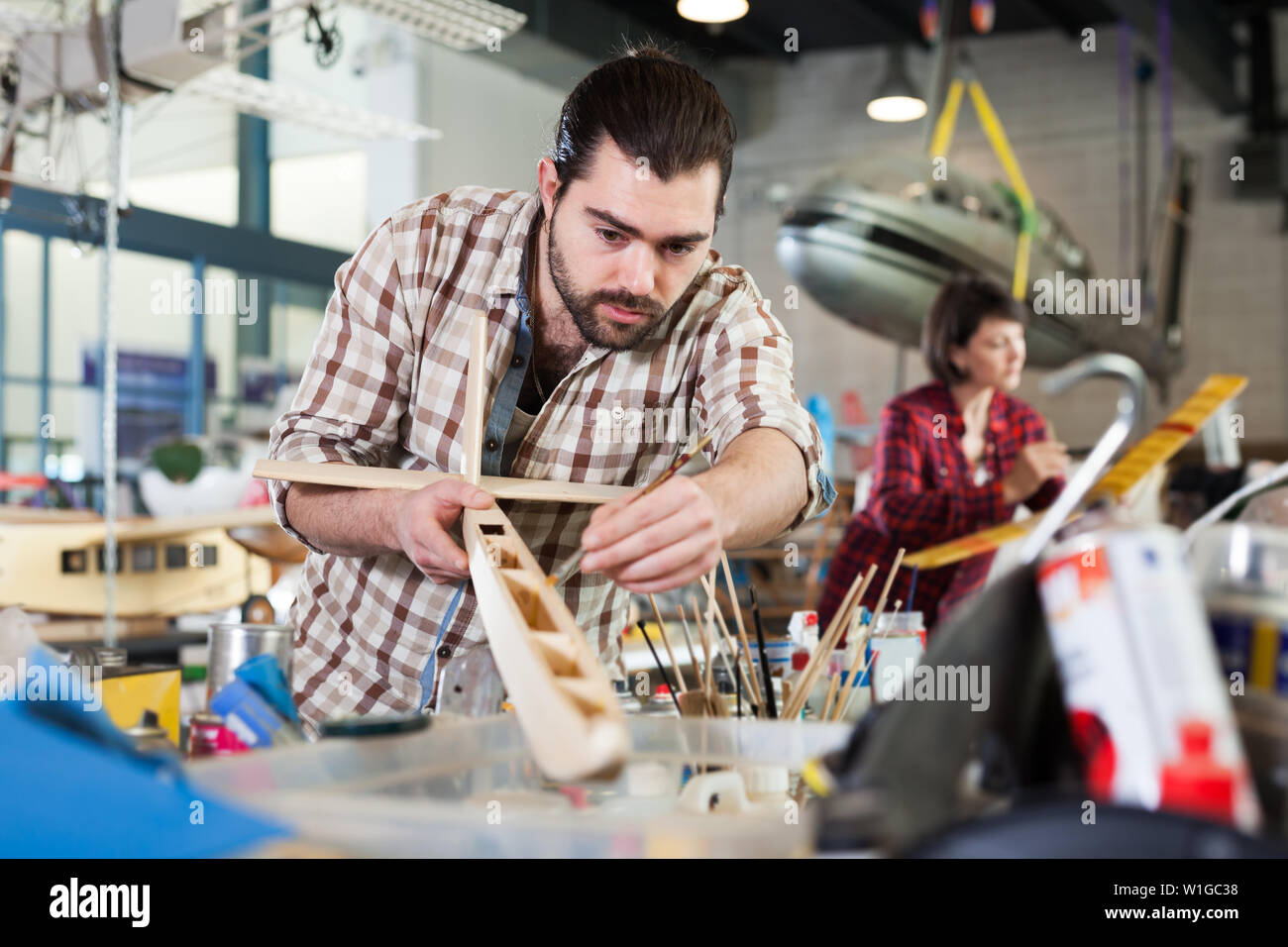 Young positive man hobbyist engaged in creating plane models in ...