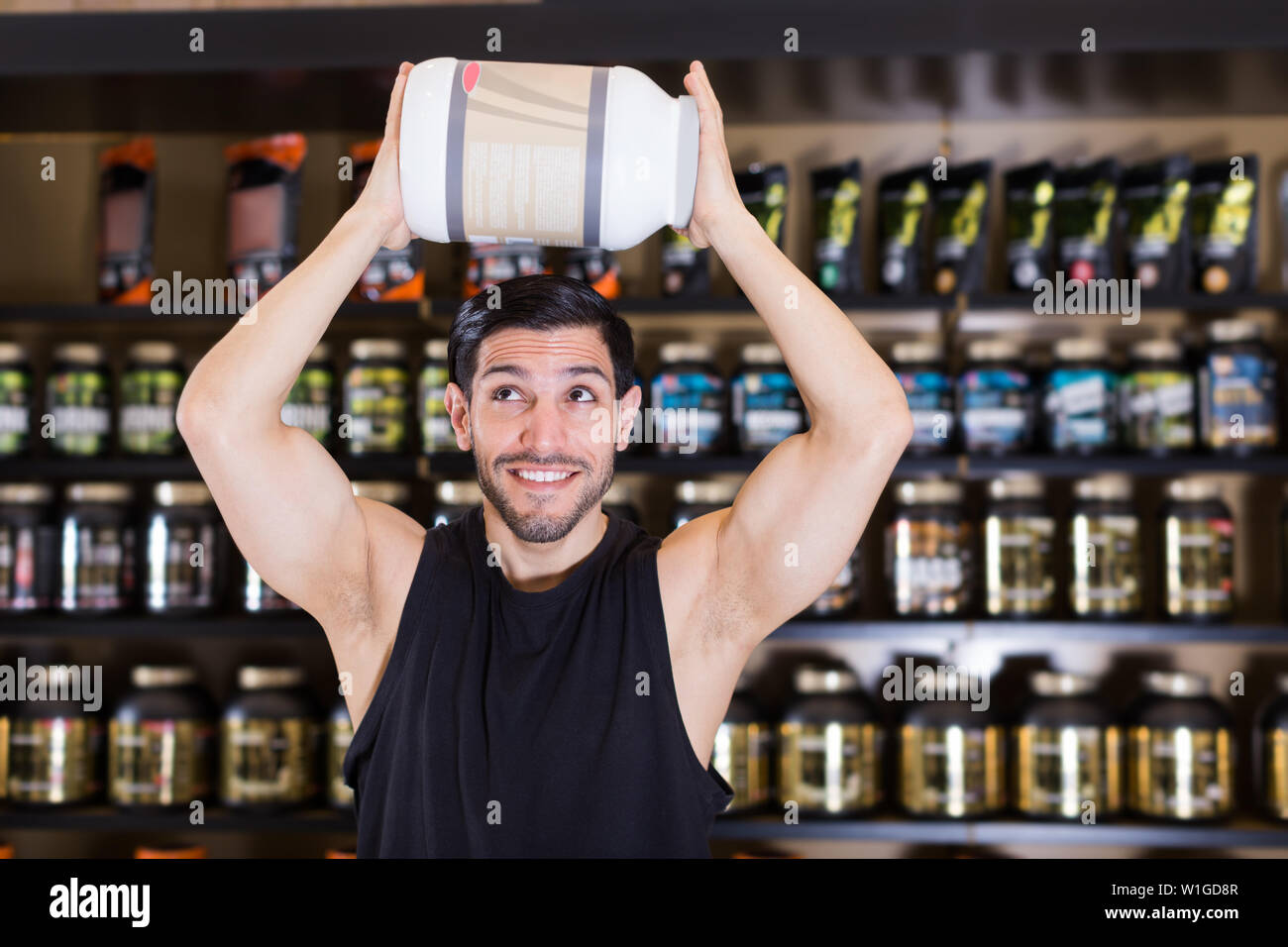 Positive man bodybuilder holding big pot of sport supplements over head ...