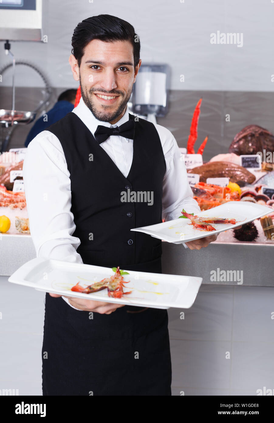Smiling waiter with seafood dishes in fish restaurant against backdrop ...