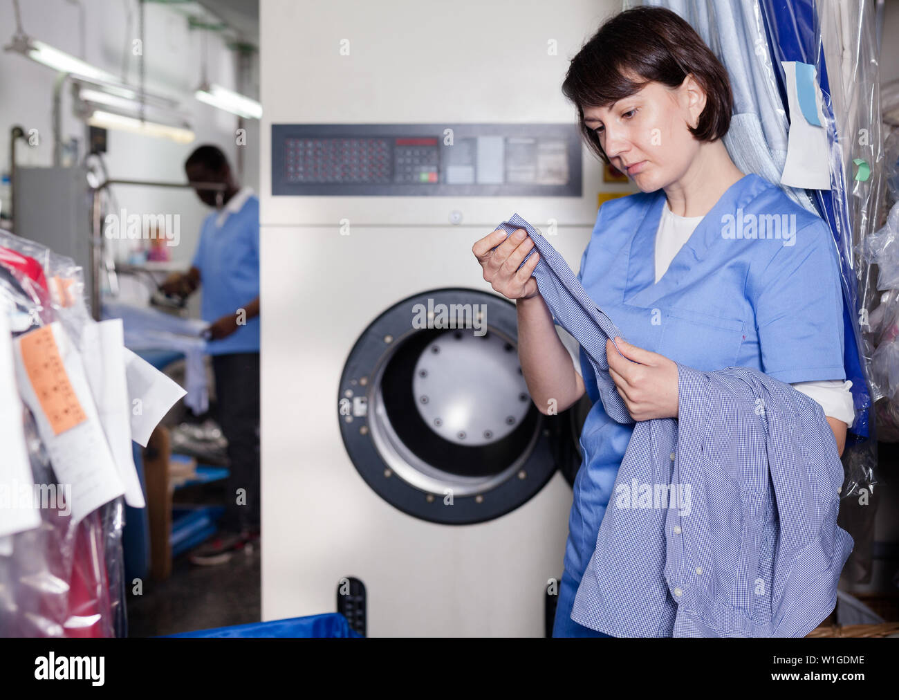 Focused female laundry worker sorting dirty clothes before dry cleaning ...