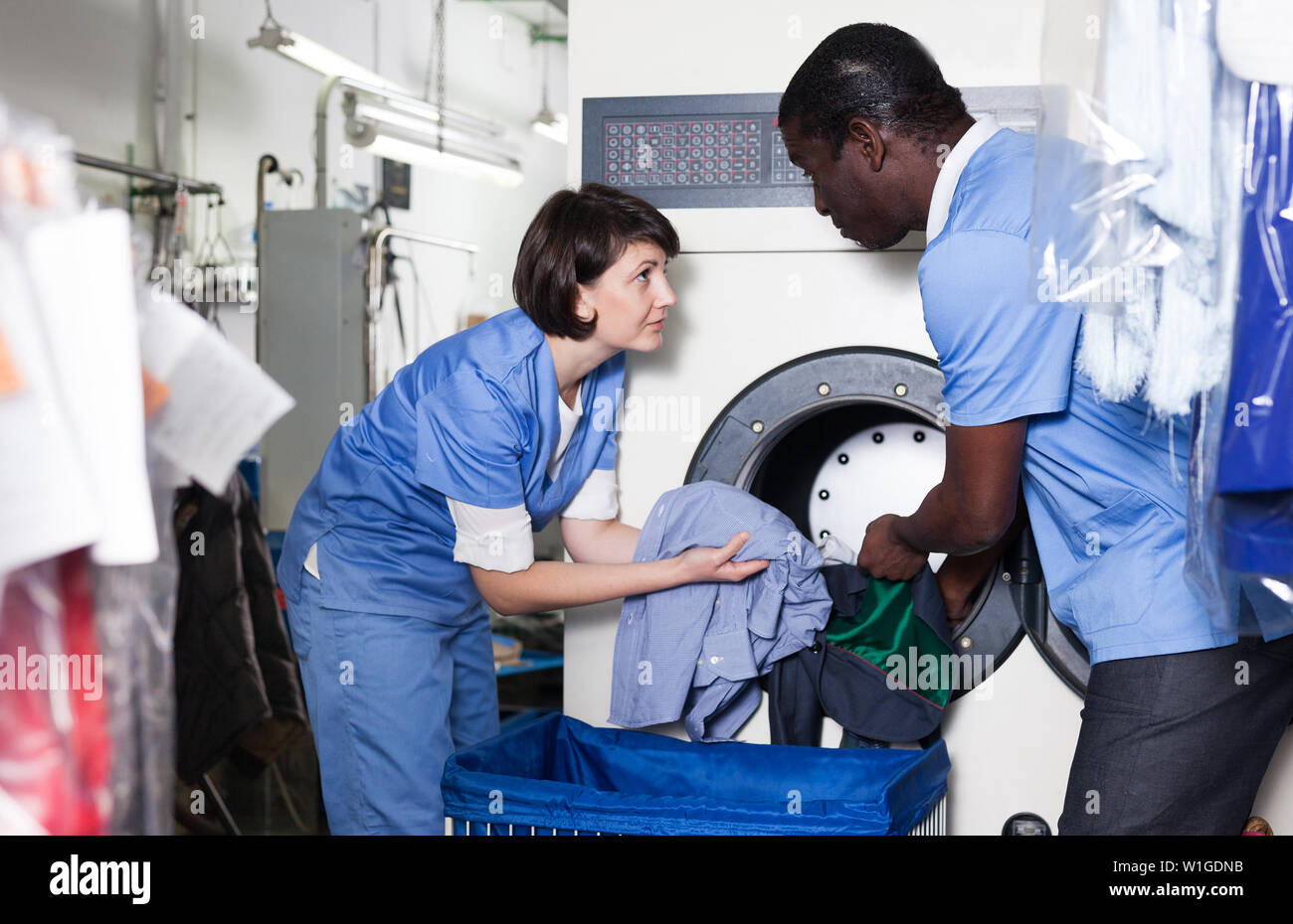 Two experienced laundry workers loading garments in washing machine for ...