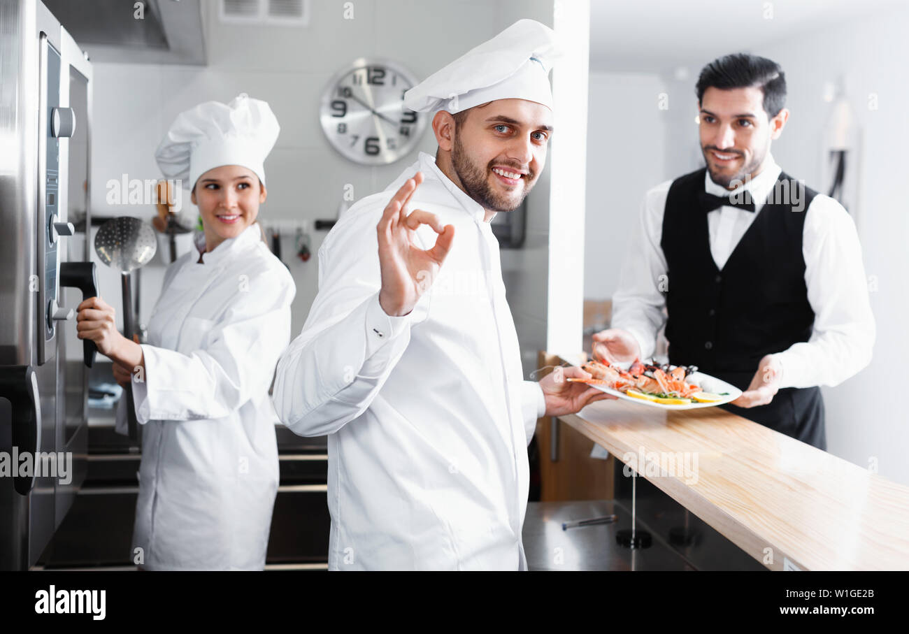 Satisfied cheerful positive male chef approving dish in kitchen of fish ...