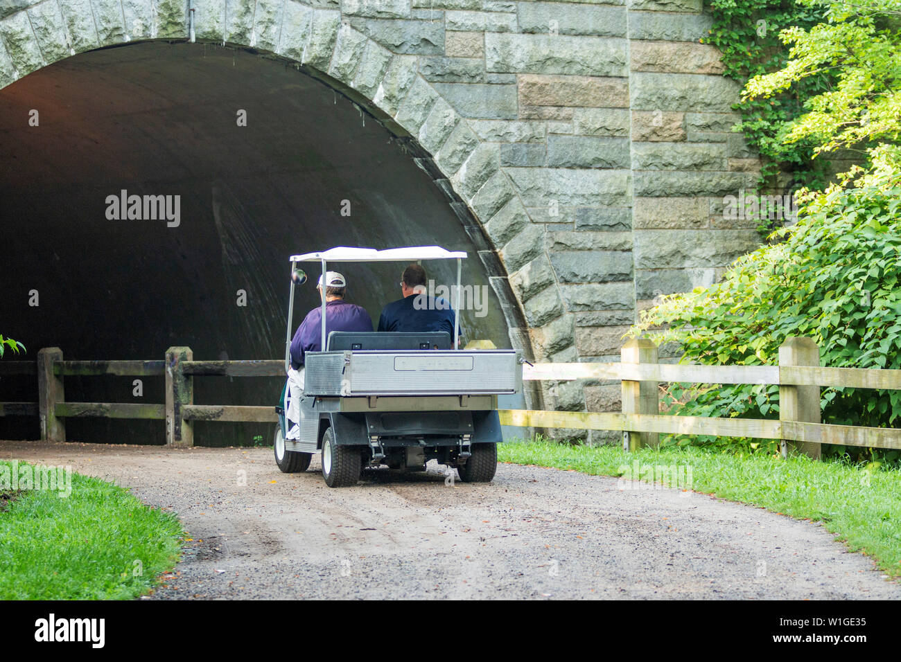A golf cart is on a dirt path heading under the sunrise highway bridge ...
