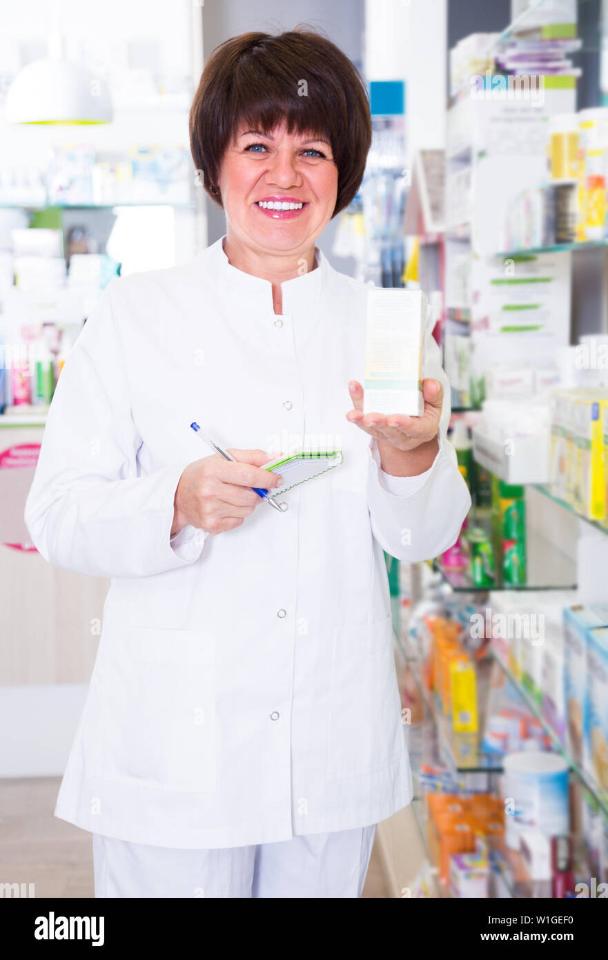 smiling pharmacist wearing uniform and selling in pharmaceutical shop ...
