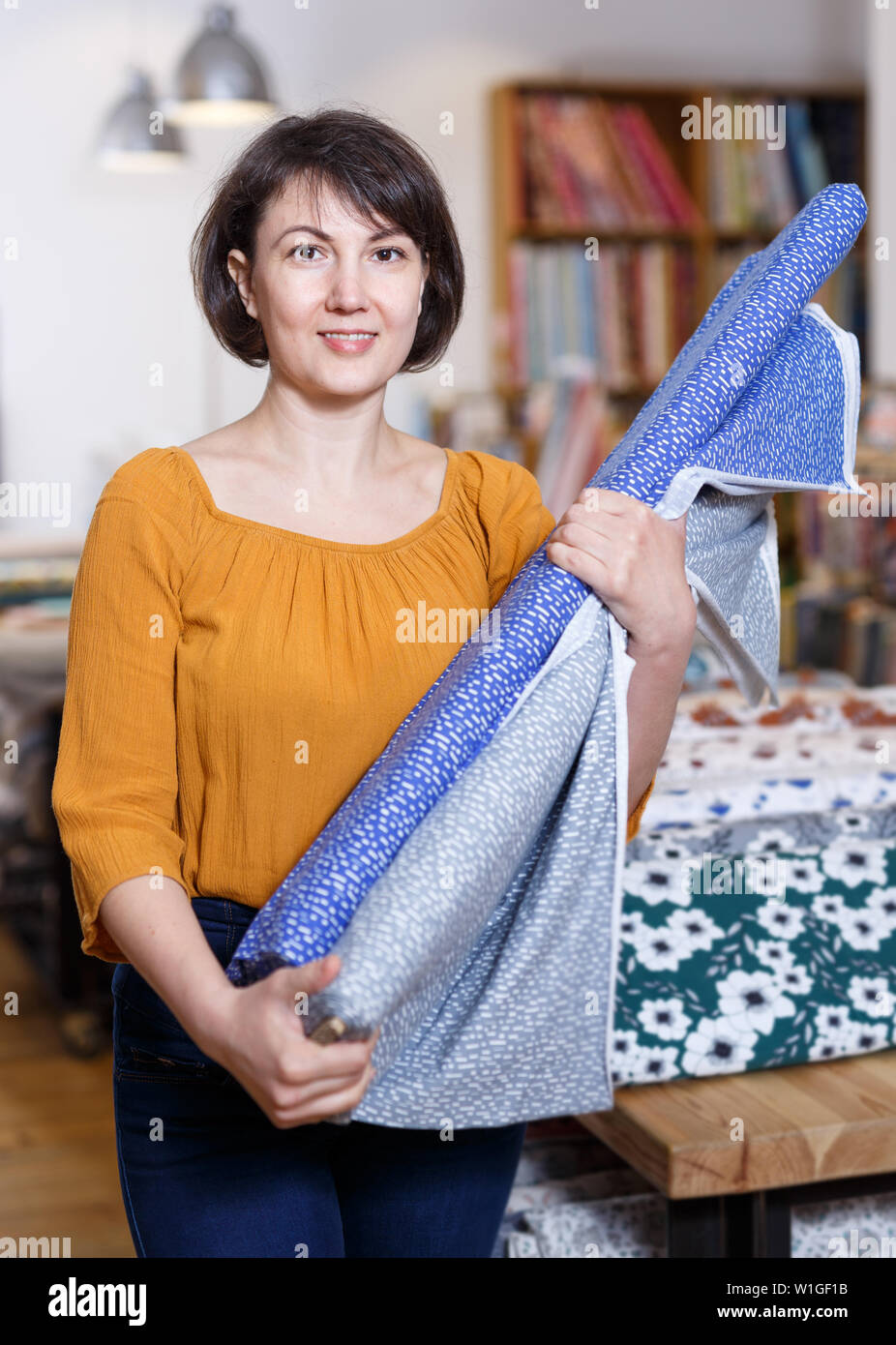 Female seller organizing assortment of textile on shelves in fabric ...