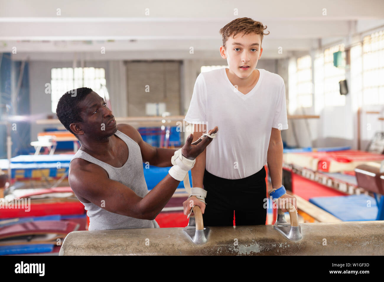 Efficient serious male coach training diligent teenage boy on gymnastic ...