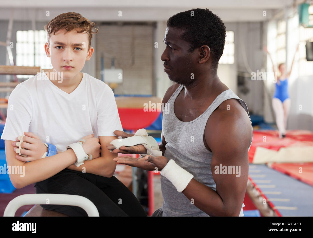 African coach soothing sad teenage athlete sitting on pommel horse at ...