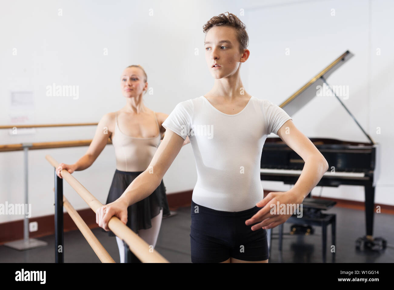 Choreographer woman and young man do exercises at ballet bar in hall ...