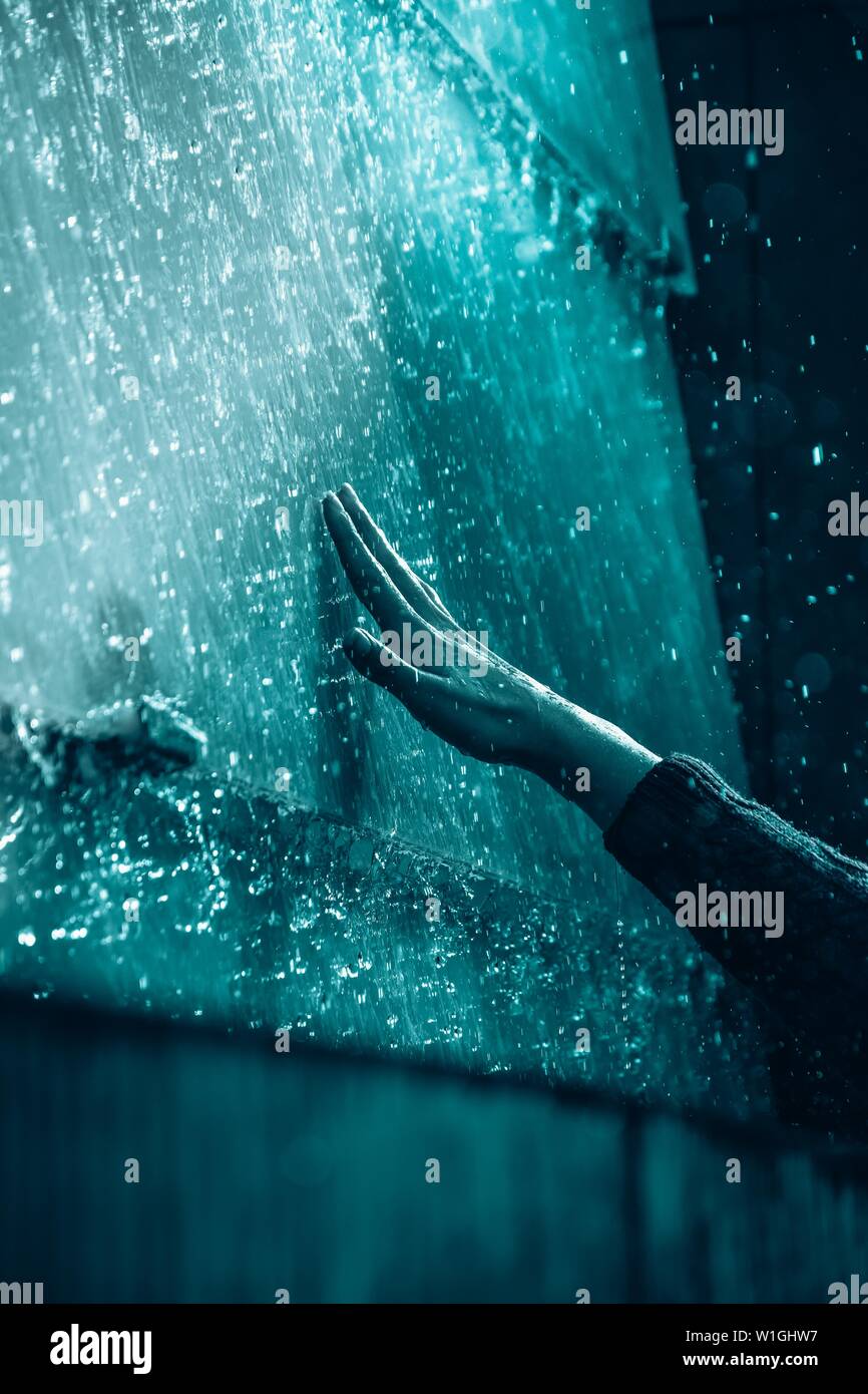 Person's hand touching a watery wall with water drips and a dark ...
