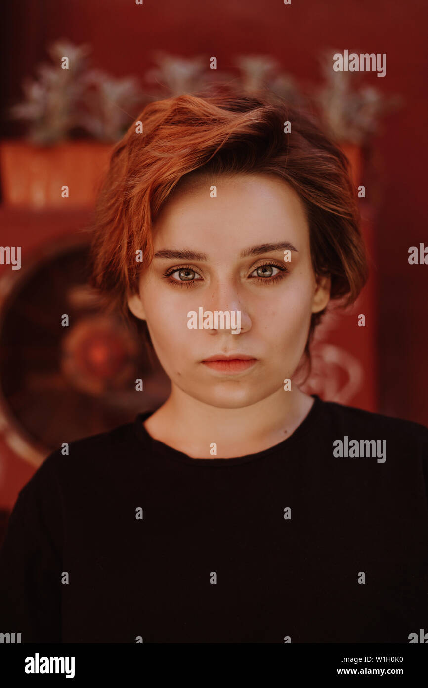 Portrait of attractive cheeky woman with short red hair at back yard in ...