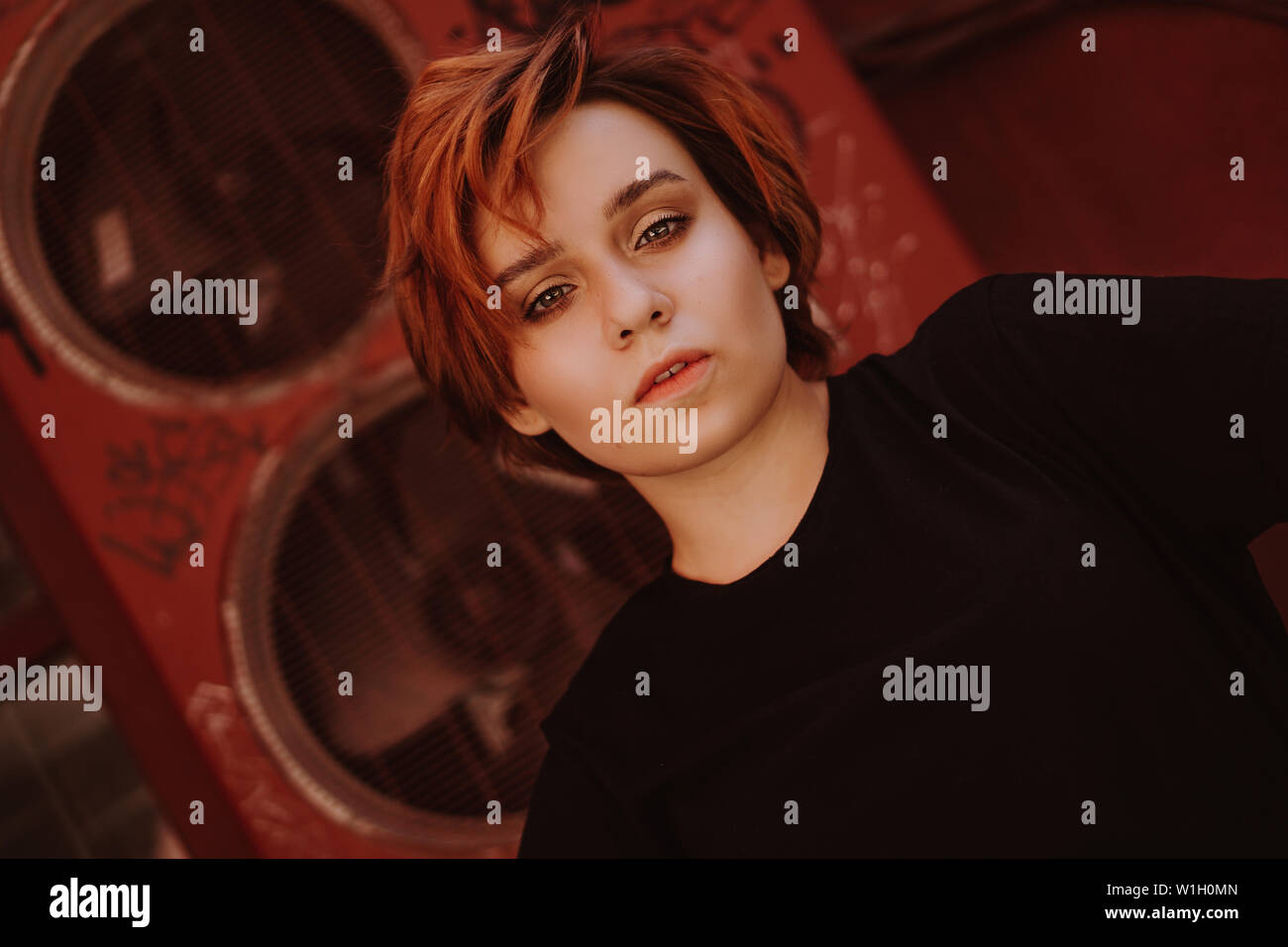 Portrait of attractive cheeky woman with short red hair at back yard in ...