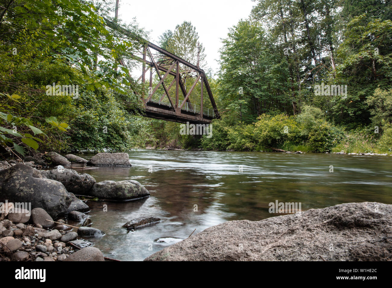 Large trestle bridge over a flowing river with a rocky bank and forest ...