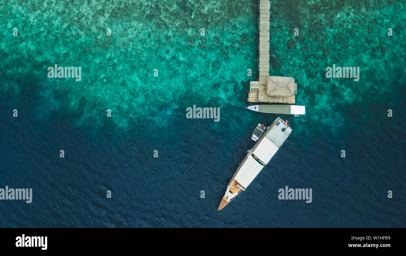 Aerial view of pier with yacht on tropical island with coral reef ...