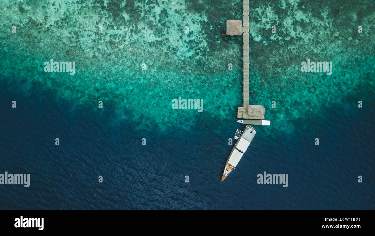 Aerial view of pier with yacht on tropical island with coral reef ...