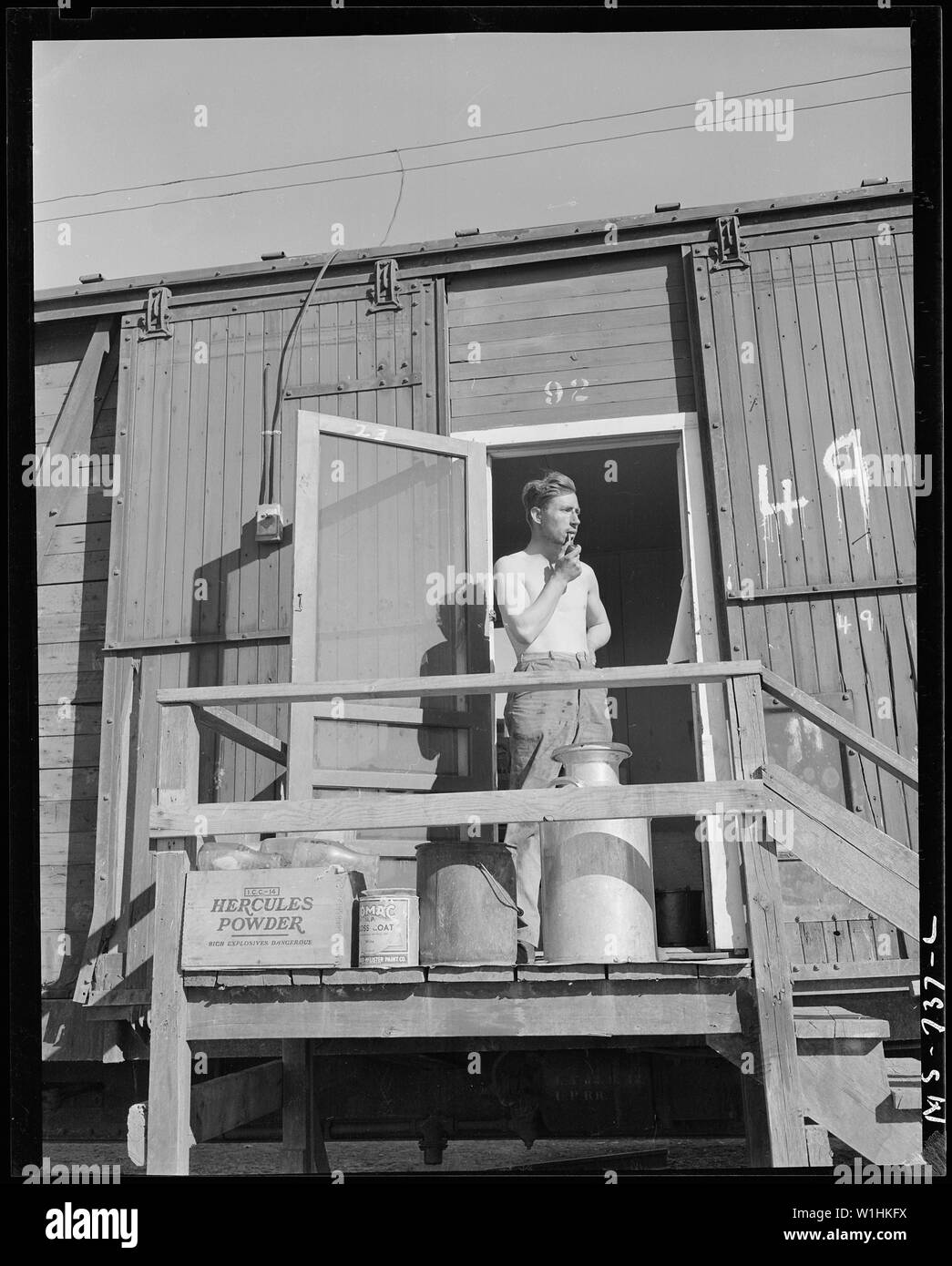 Patsy Howard, miner, standing on porch of his box car home in company ...
