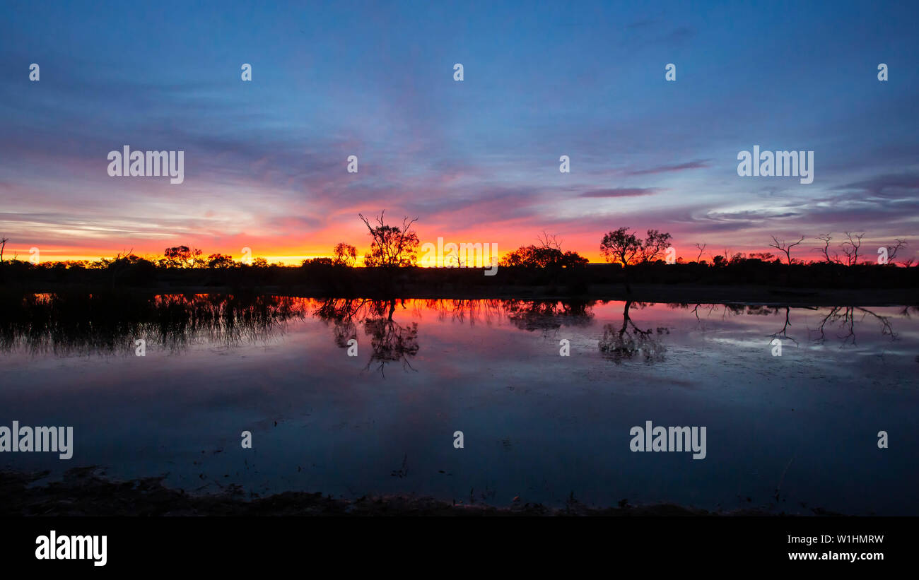 Dramatic sky, trees in silhouette and reflections on water at dusk in ...