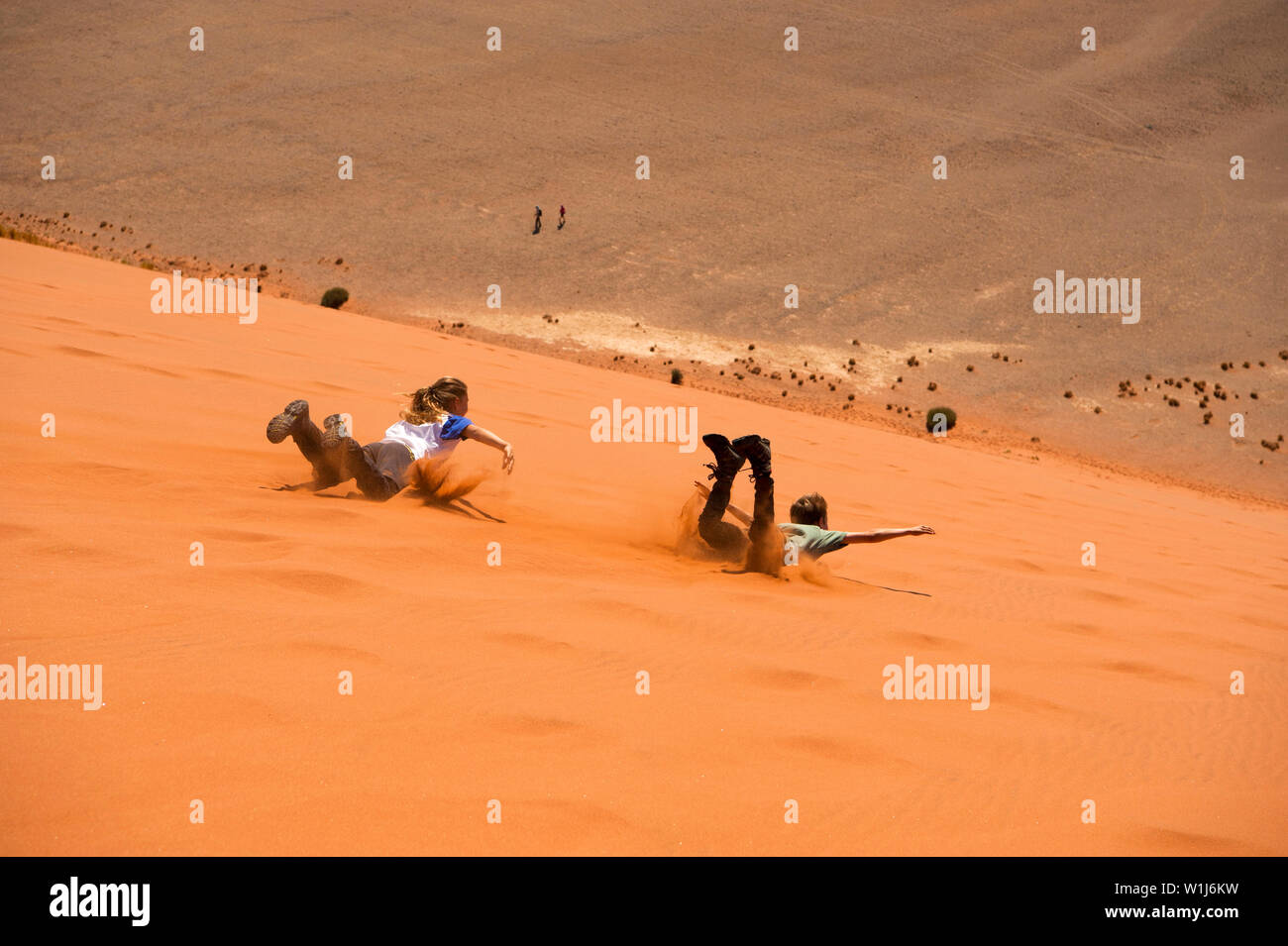 Hikers dune surfing down a sand dune at Sossusvlei, Namib-Naukluft ...