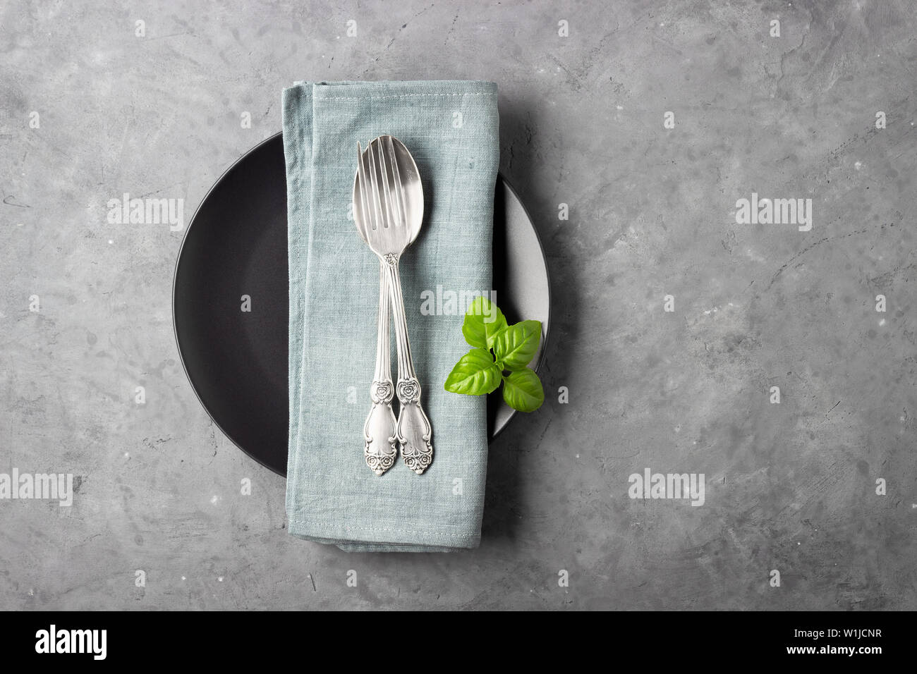 Table setting. Black plate, cutlery and napkin over gray concrete ...