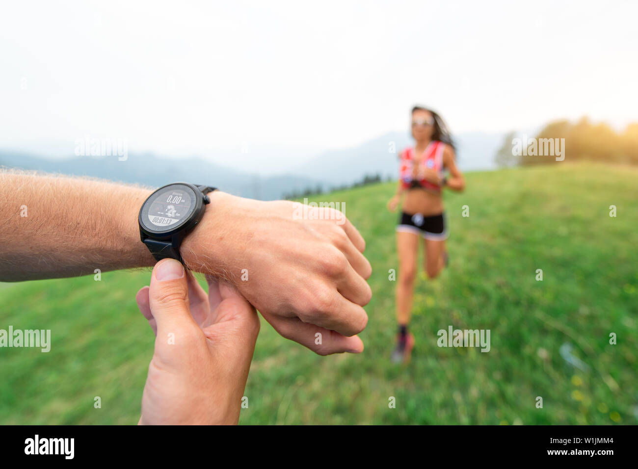 Athletic trainer holds the stopwatch while training a girl running in ...