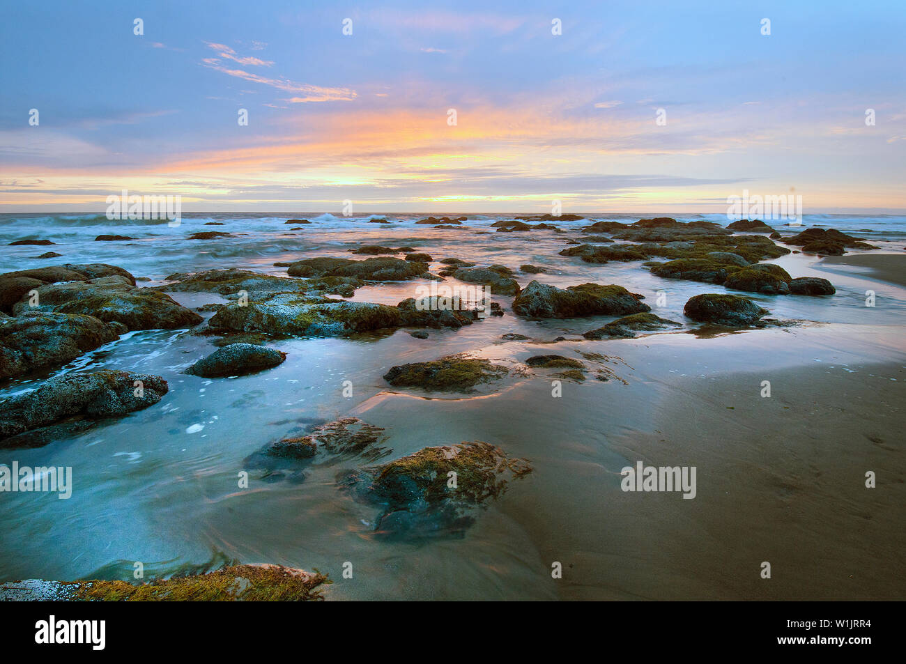 The Pacific tide rolls over rocks and onto the shorline on a beach in ...