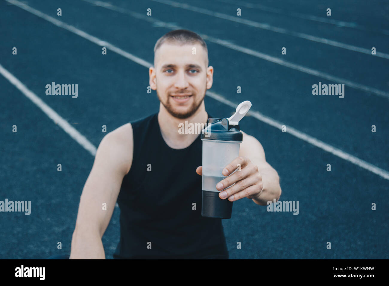 muscular slender man in training at the stadium drinks water from a ...