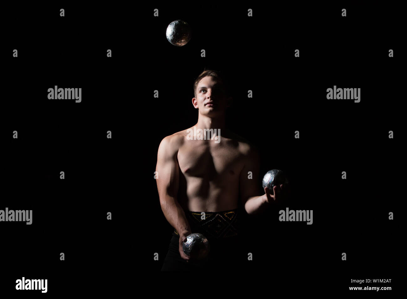 Handsome guy with a muscular body juggles with heavy balls on a black ...